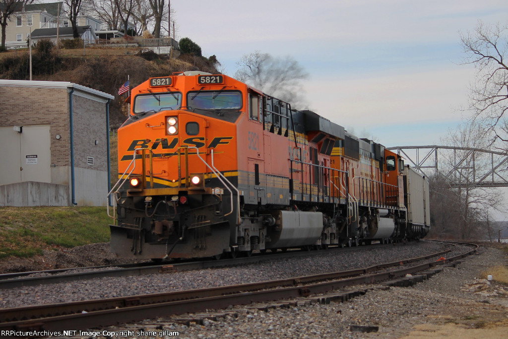 BNSF 5821 leads a wb coal train down river front.